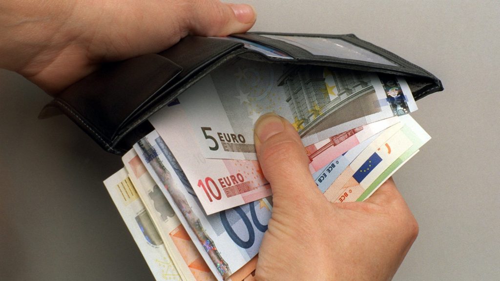 Eine-maennliche-Hand-steckt-mehrere-Geldscheine-in-ein-Portmonnaie ...